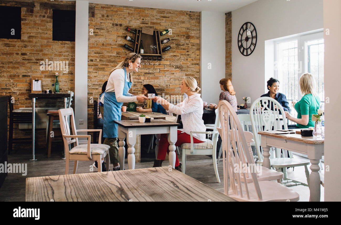 Waitress is serving a cup of tea to a customer sitting at a table in a ...