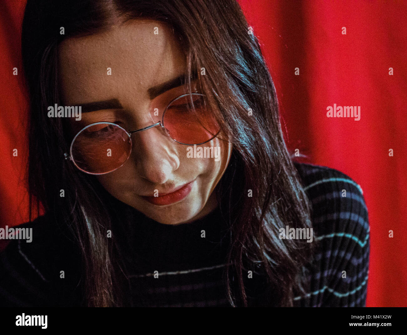 Girl looking down with a red/pink backdrop Stock Photo - Alamy