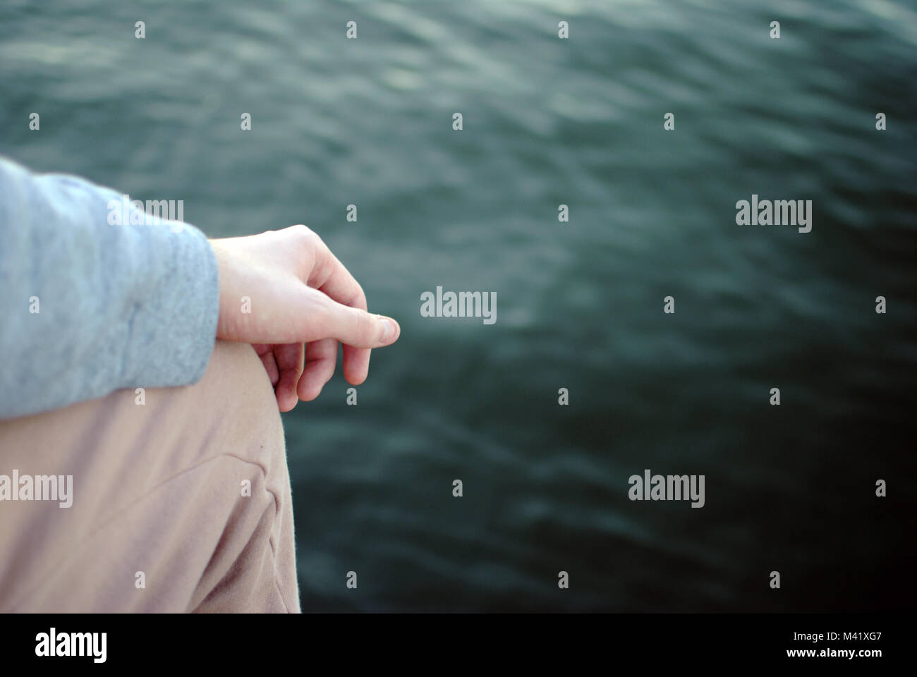 mans arm resting on his leg with a water backdrop Stock Photo - Alamy