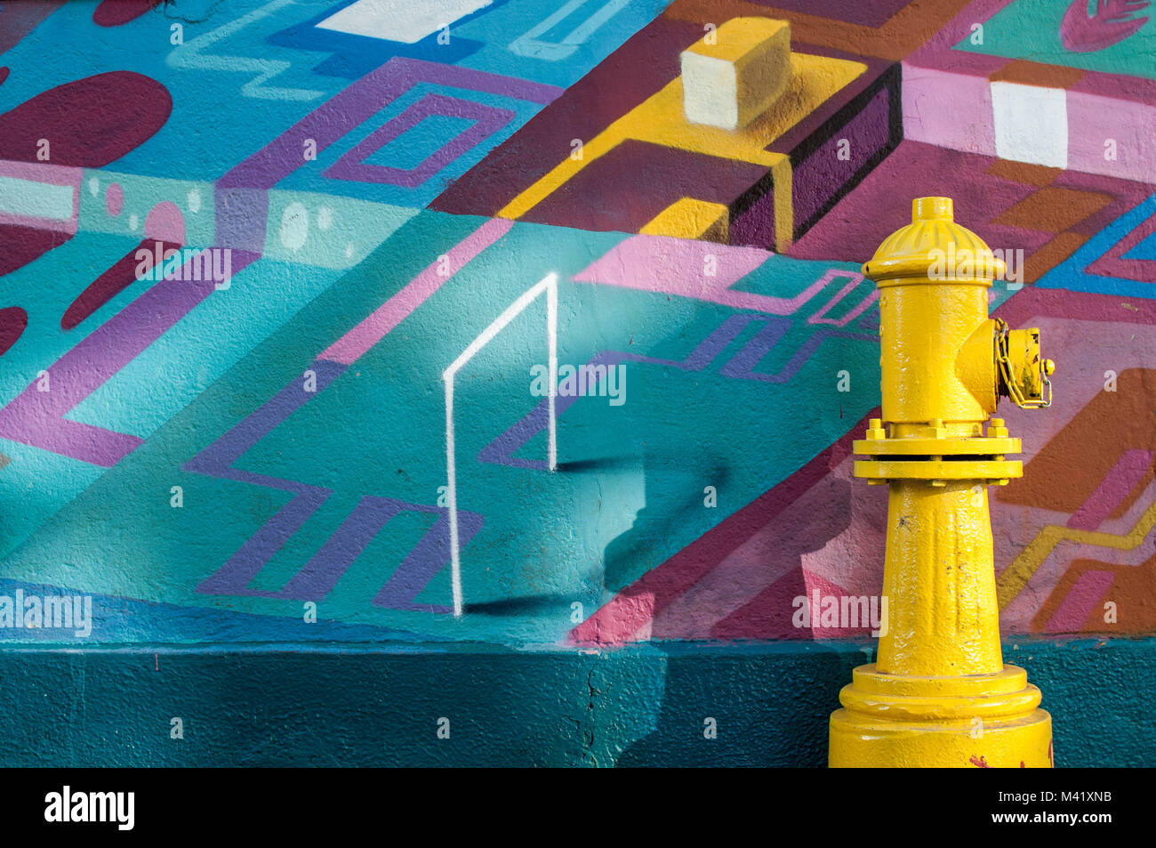 A bright yellow fire hydrant in front of a colorful painted mural on a ...