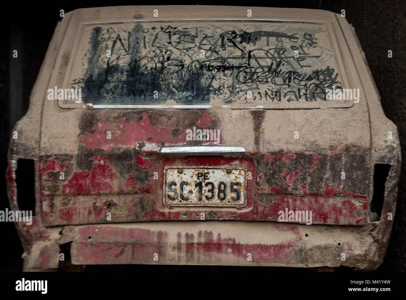 A rusty and dented old red car with Peruvian license plate words ...