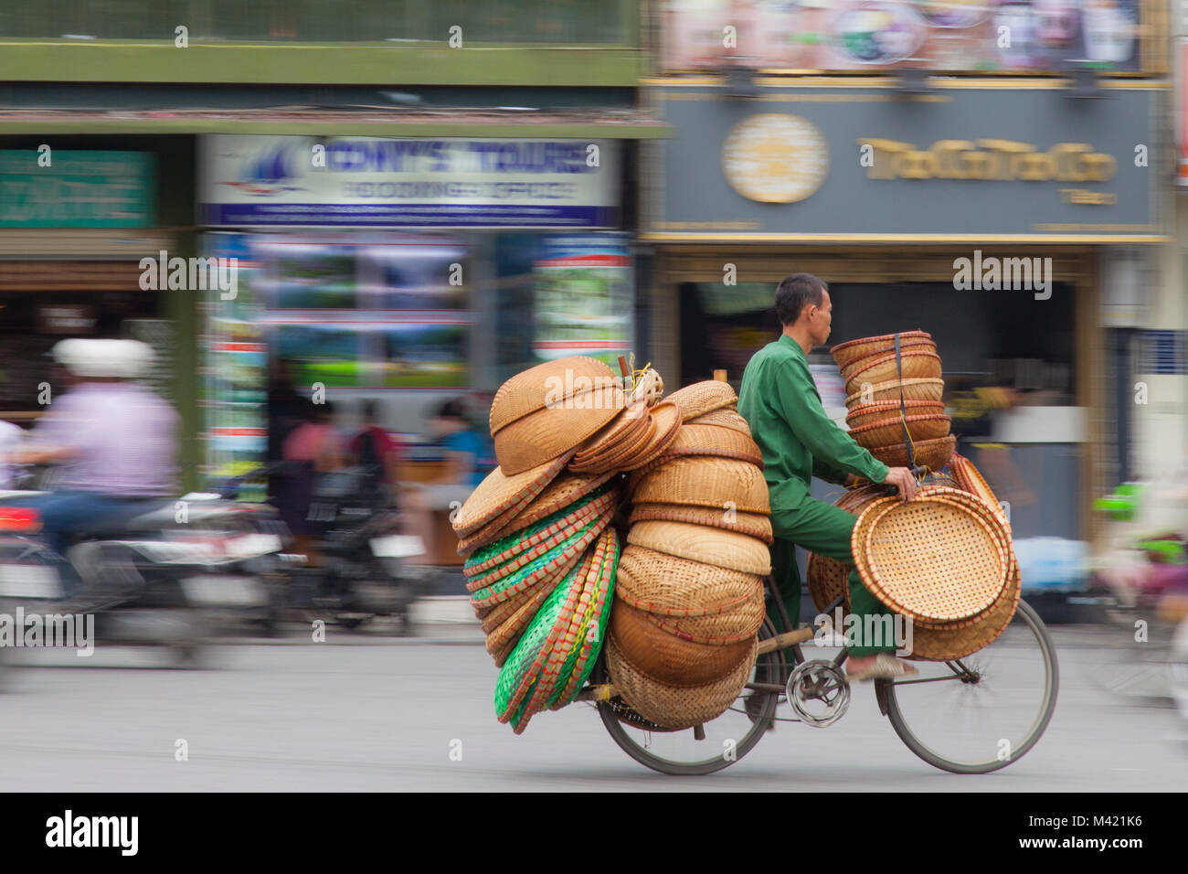 man with baskets riding his bicycle across busy street in Hanoi ...