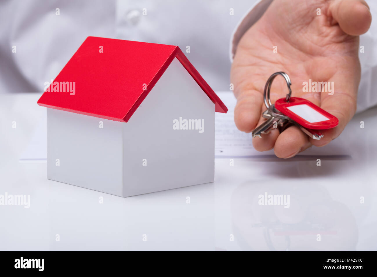 Human Hand Holding House Keys With House Model On Desk Stock Photo - Alamy
