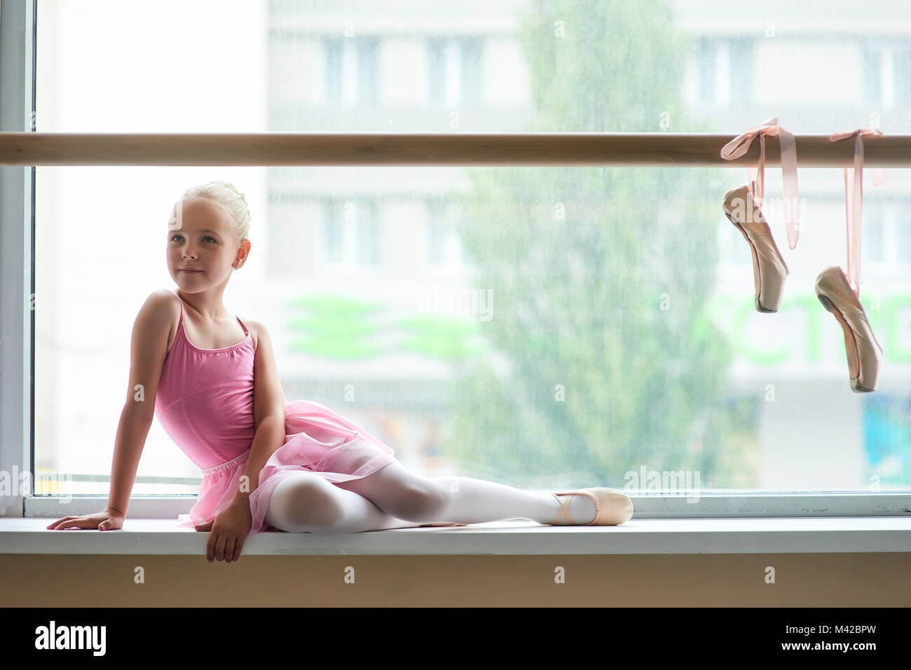 Lovely little ballerina posing at window-sill. Beautiful ballet dancer ...