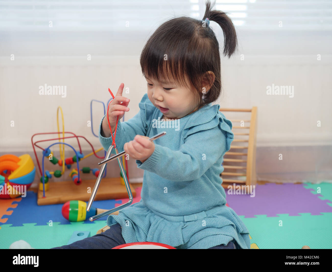 baby girl play triangle at home Stock Photo - Alamy