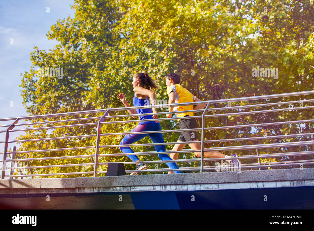 Side view portrait of active young people running across a bridge as ...