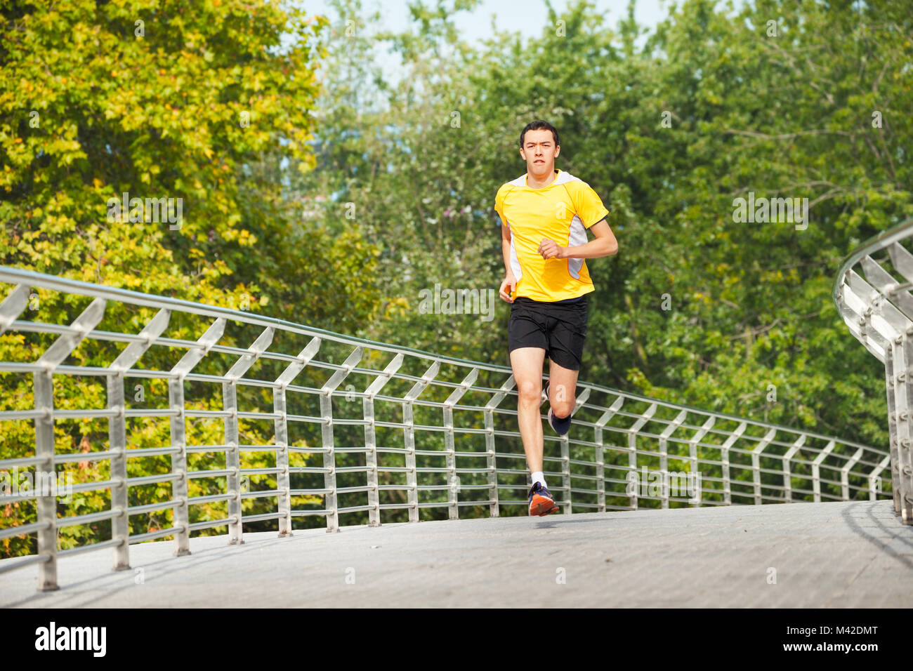 Sporty young man running alone on bridge at sunny day Stock Photo - Alamy
