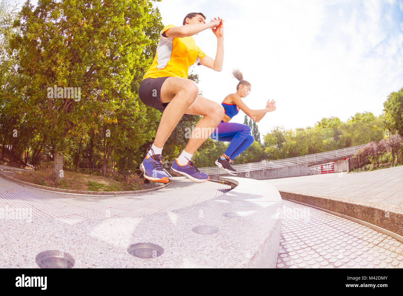 Sporty young man and woman jumping on border at crossfit style outdoors ...
