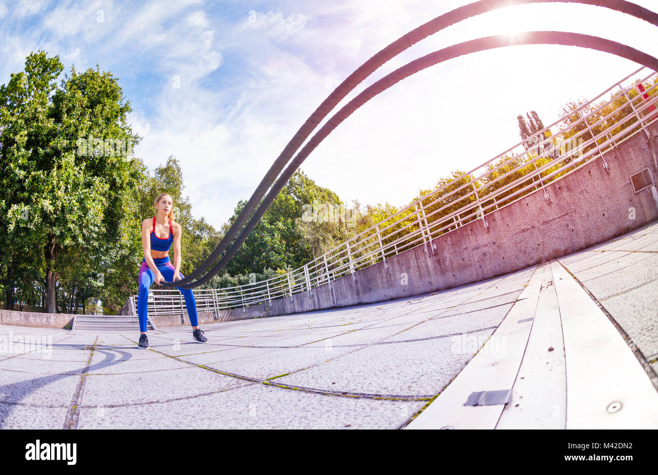 Young woman making wave movement with muscle rope during crossfit ...