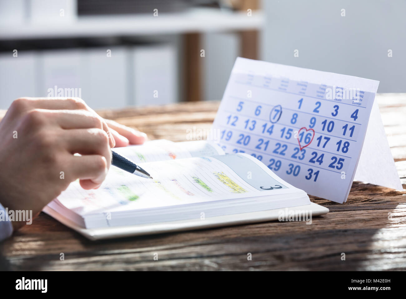 Businessperson's Hand Checking Schedule In Diary With Calendar On ...