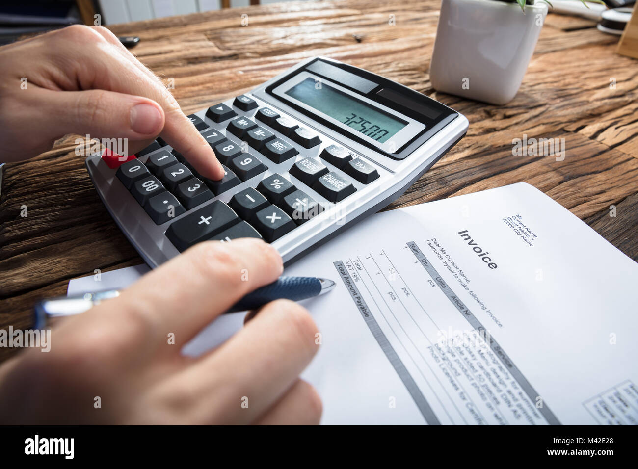 A Person's Hand Calculating Invoice With Calculator On Wooden Desk ...
