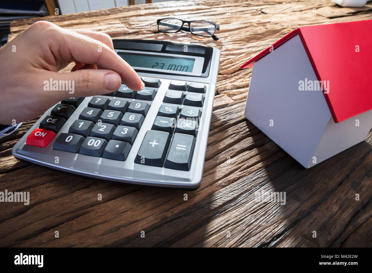 Person's Hand Using Calculator With House Model On Wooden Desk Stock ...