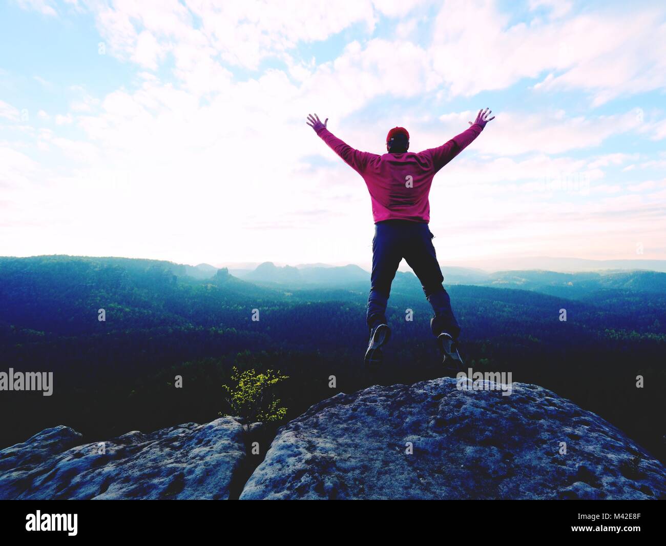 Jumping man. Young crazy man is jumping on rocky summit above landscape ...