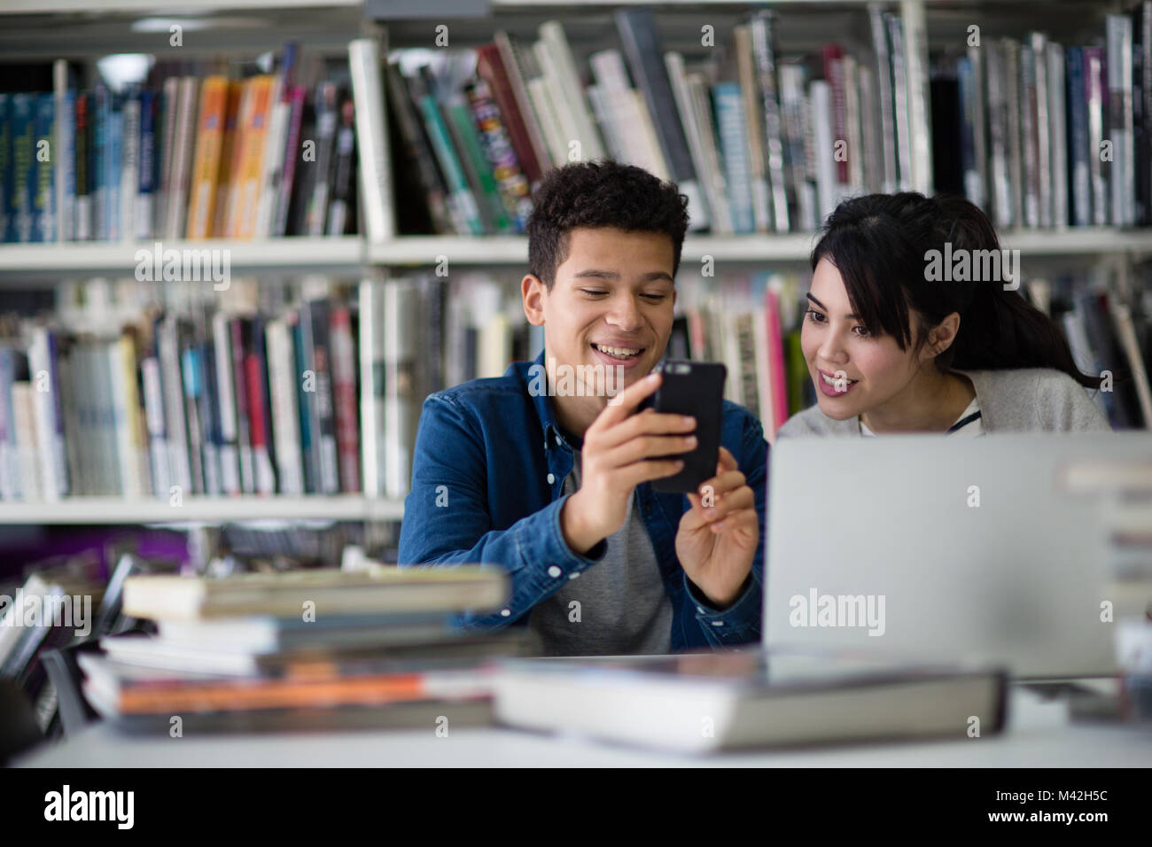 Students looking at smartphone in library Stock Photo - Alamy