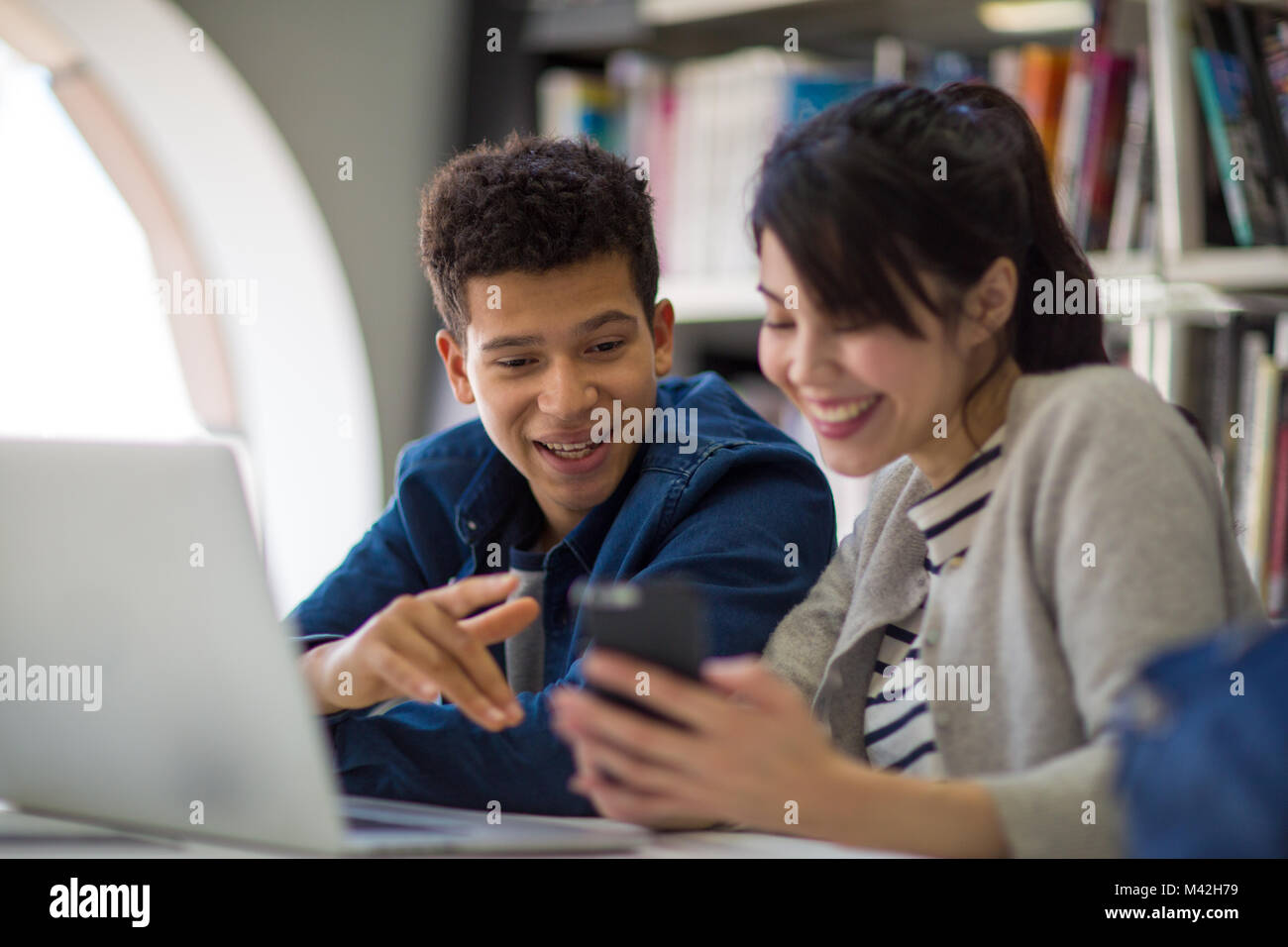 Students looking at smartphone in library Stock Photo - Alamy