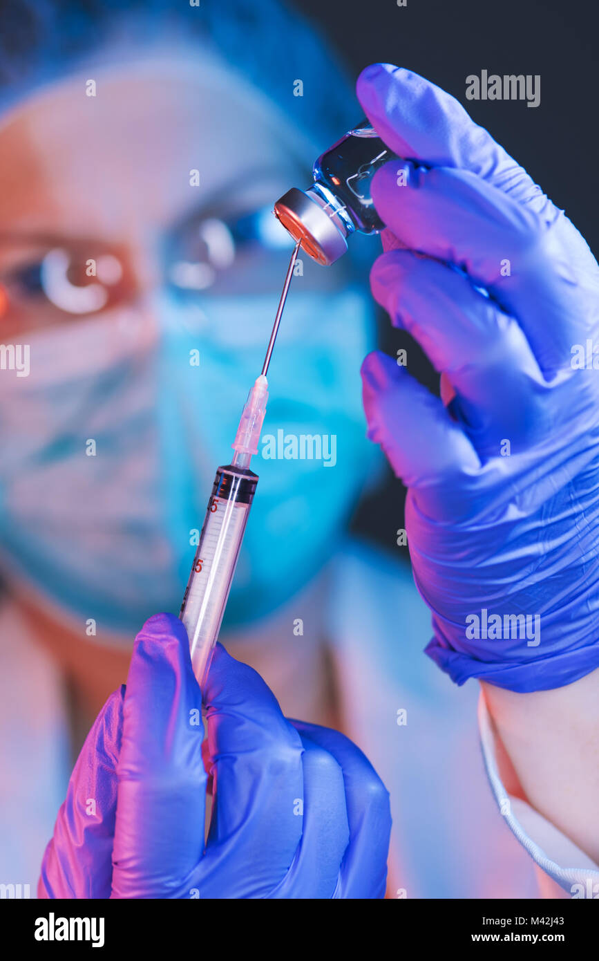 Doctor drawing up solution from vaccine bottle and filling syringe ...