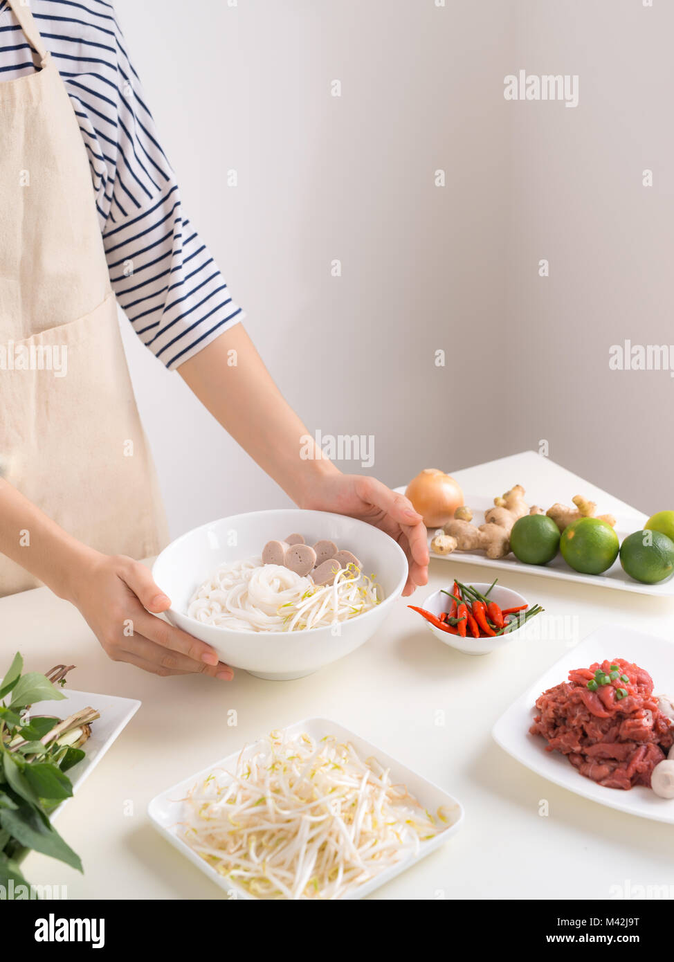 Female chef prepare traditional Vietnamese soup Pho bo with herbs, meat ...