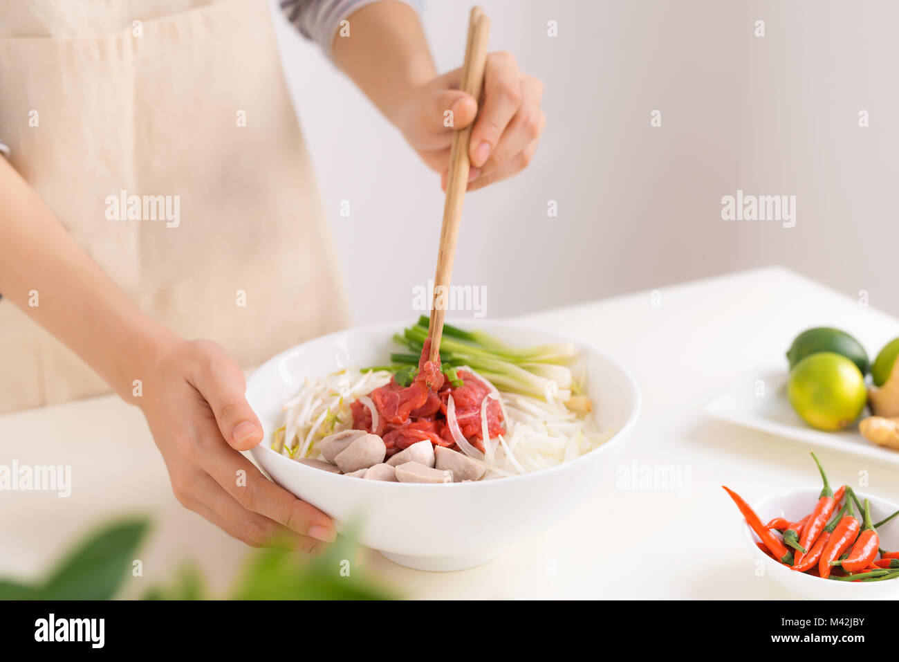 Female chef prepare traditional Vietnamese soup Pho bo with herbs, meat ...