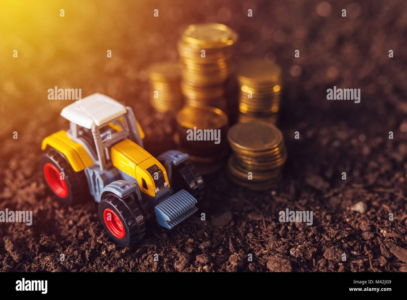 Agricultural tractor toy and golden coins on fertile soil land, income ...