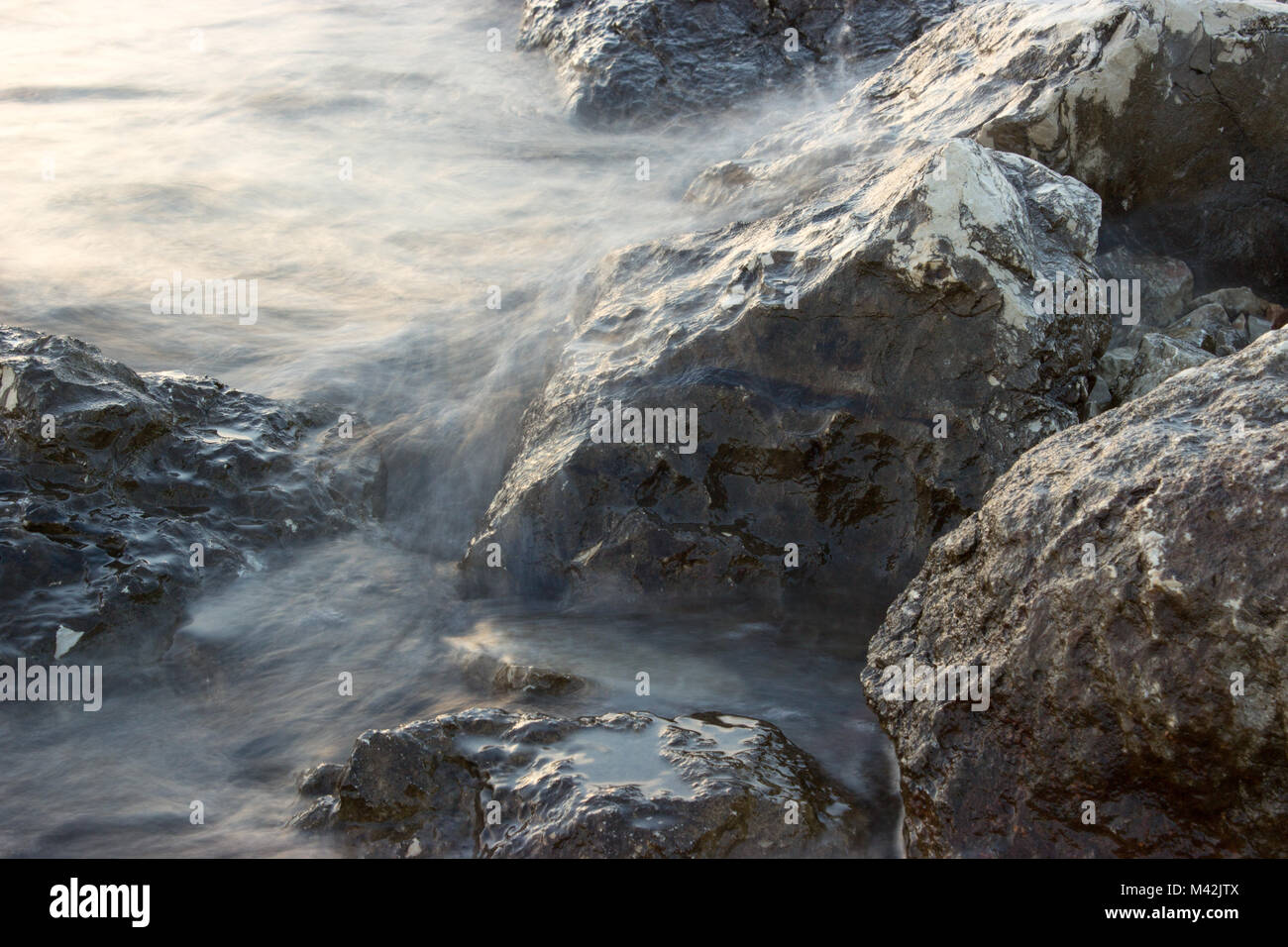 The rocks emerging from the sea are illuminated by the setting sun ...