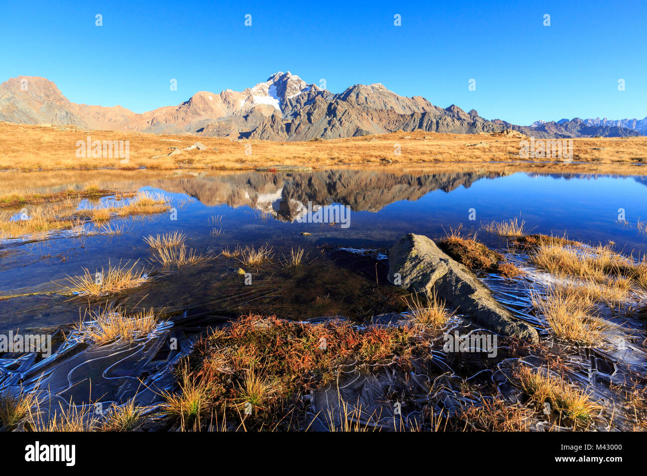 Rocky peaks of Mount Disgrazia are reflected in the alpine lake Val ...