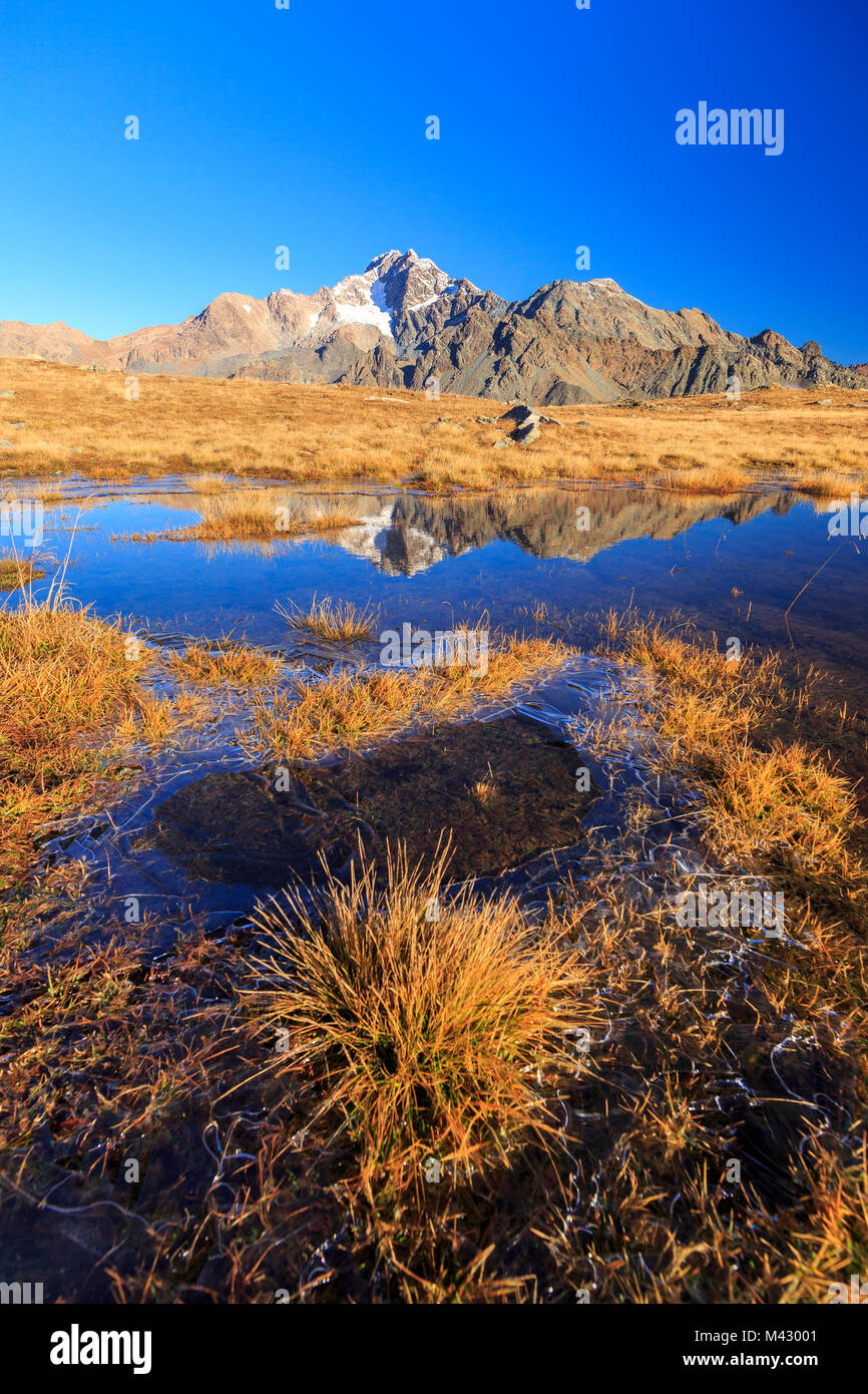 Rocky peaks of Mount Disgrazia are reflected in the alpine lake Val ...