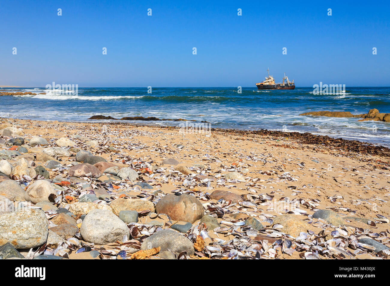 Ship in the ocean framed by shells and rocks on the sand shore Walvis ...