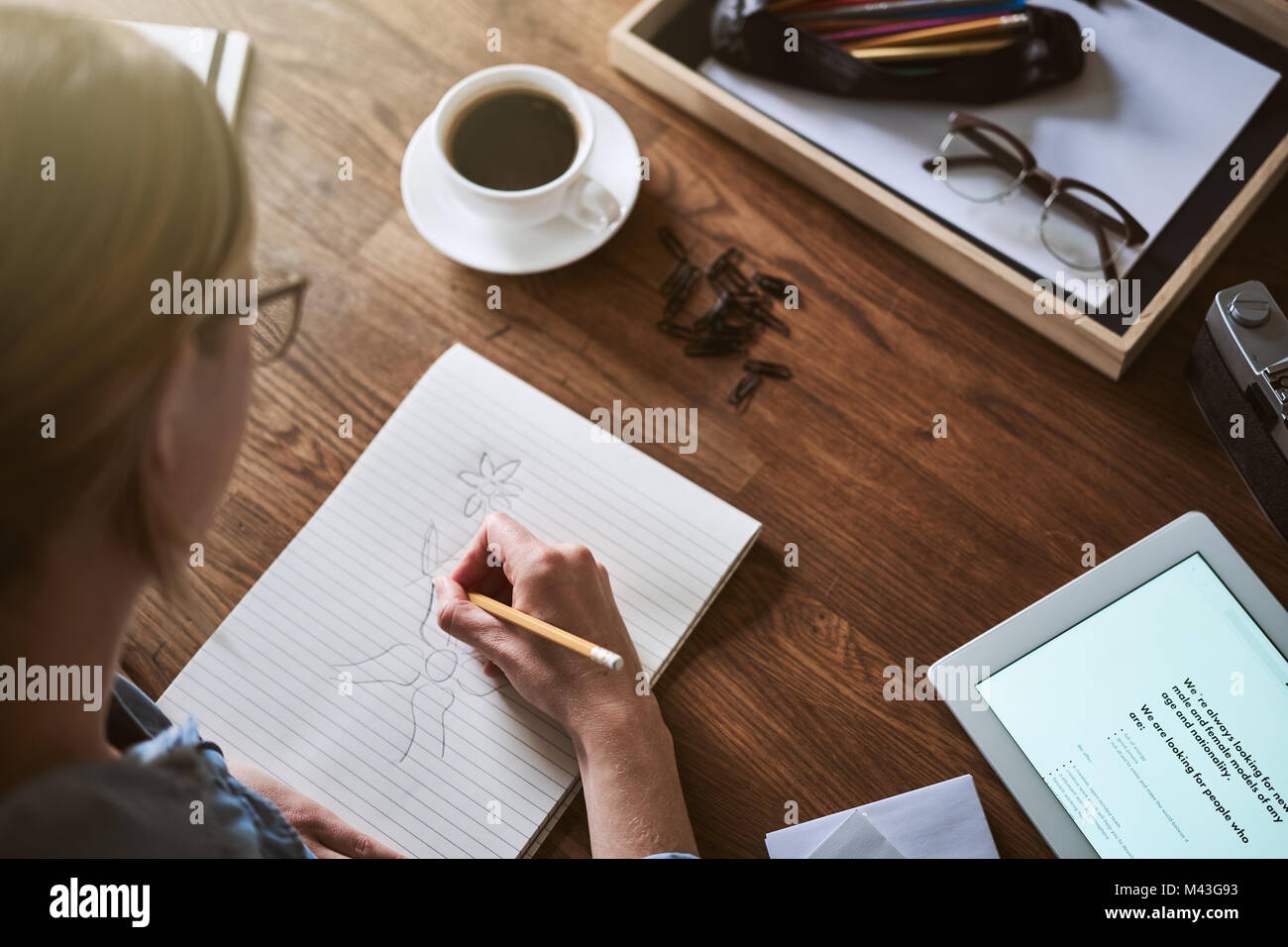 Young woman sitting at a table at home sketching out designs with a ...