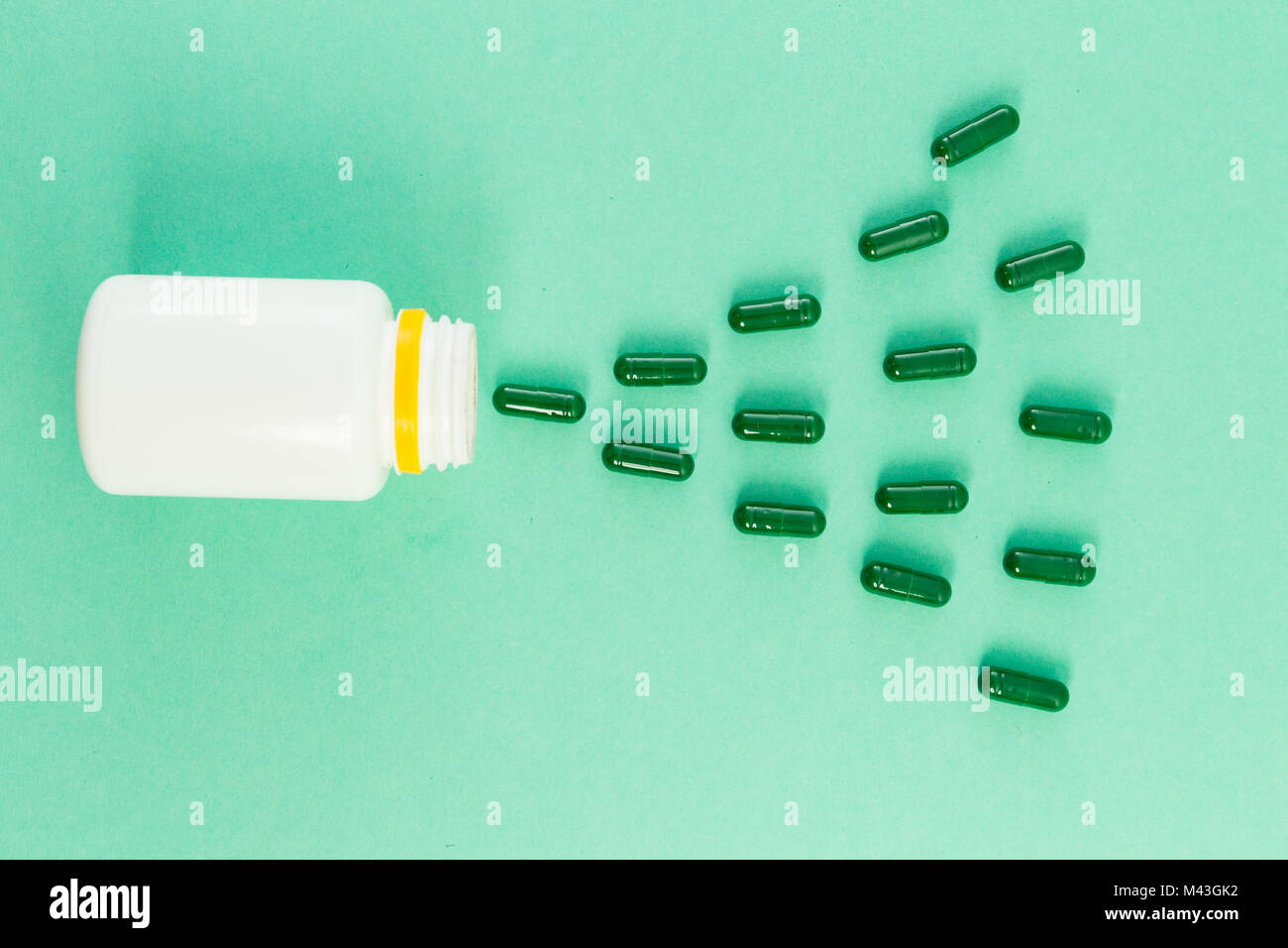 Green pills or tablets spilled as a pattern from a plastic drugs bottle ...