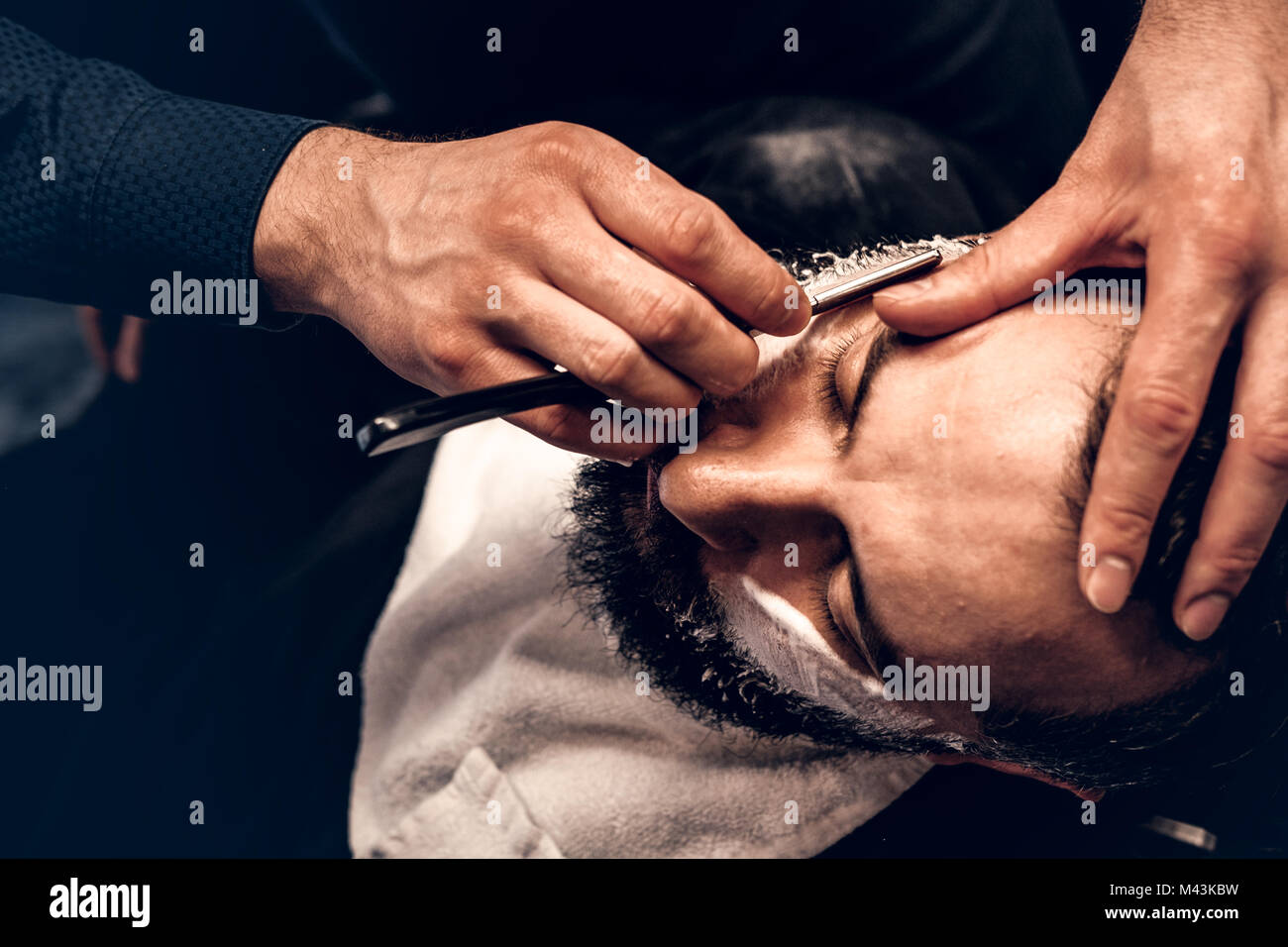 Barber shaving bearded male with a sharp razor Stock Photo - Alamy
