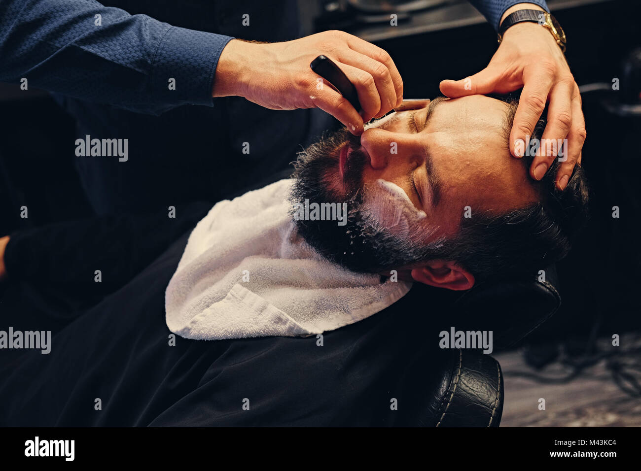 Barber shaving bearded male with a sharp razor Stock Photo - Alamy