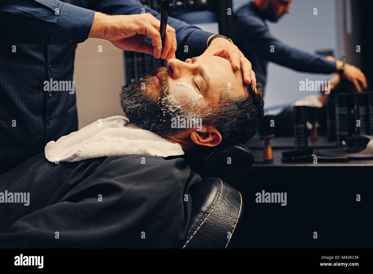 Barber shaving bearded male with a sharp razor Stock Photo - Alamy