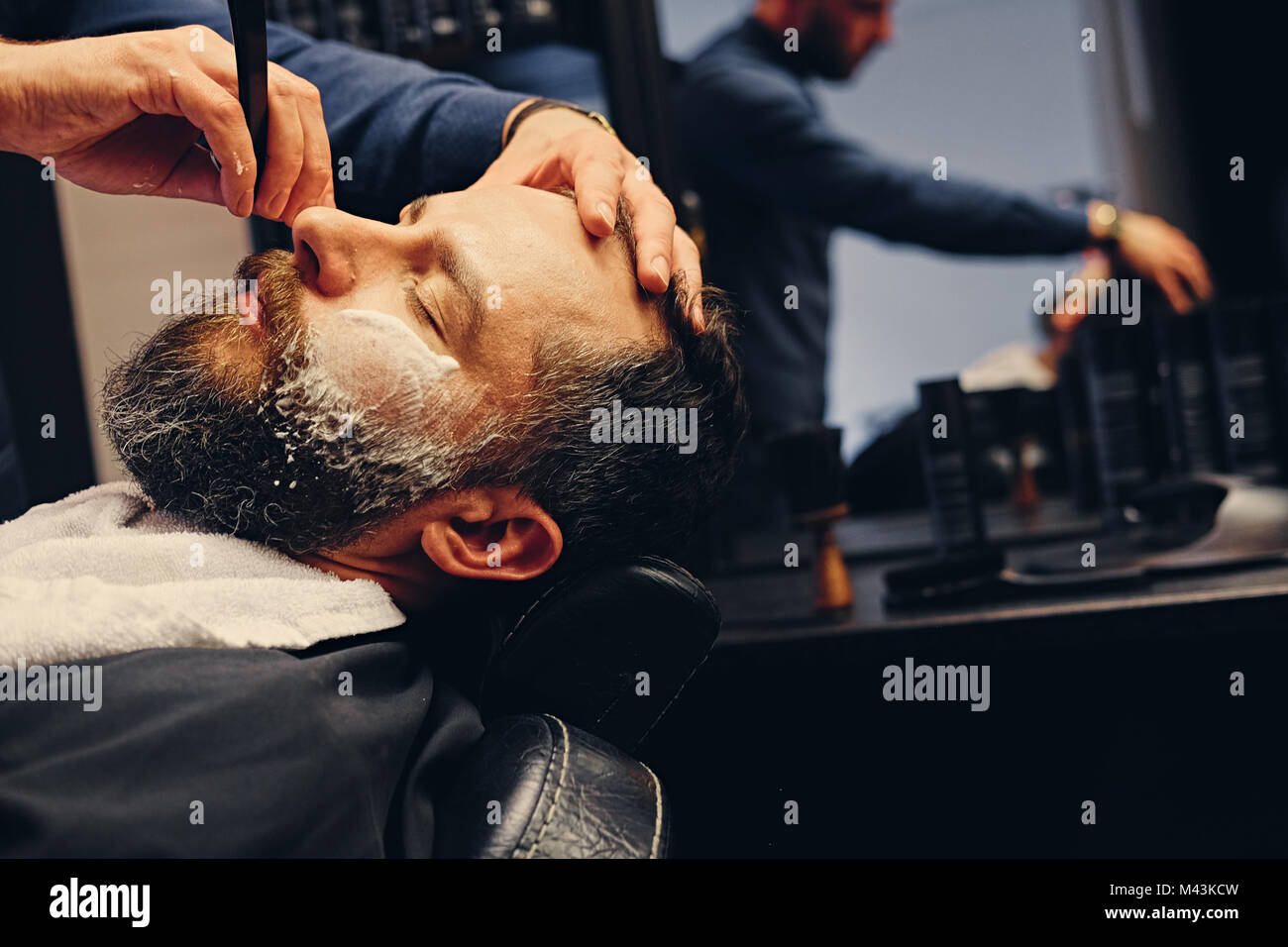 Barber shaving bearded male with a sharp razor Stock Photo - Alamy