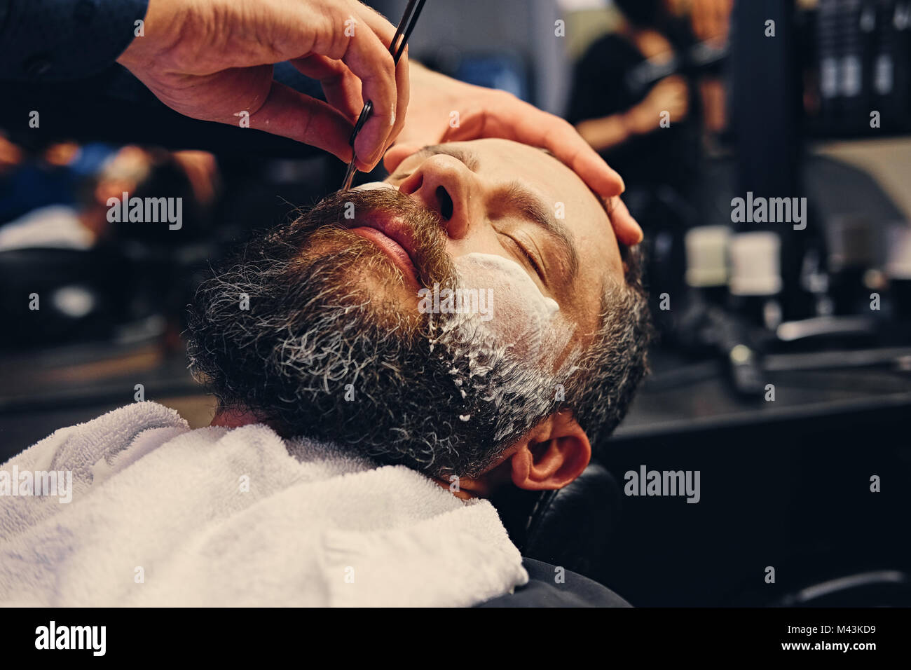 Barber shaving bearded male with a sharp razor Stock Photo - Alamy