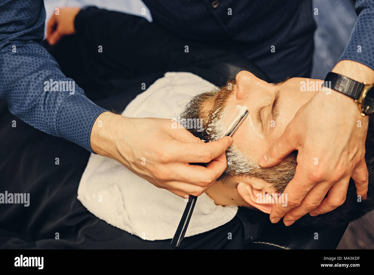 Barber shaving bearded male with a sharp razor Stock Photo - Alamy