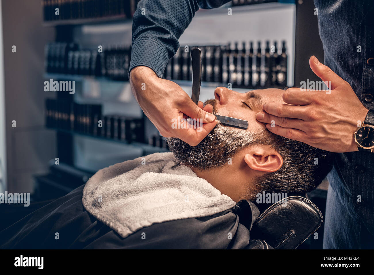 Barber shaving bearded male with a sharp razor Stock Photo - Alamy