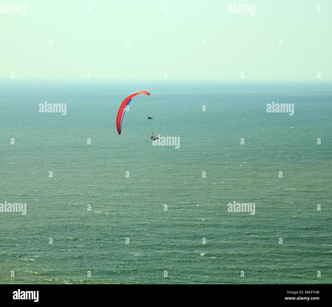 Red paraglider flying in blue sky over the ocean Stock Photo - Alamy