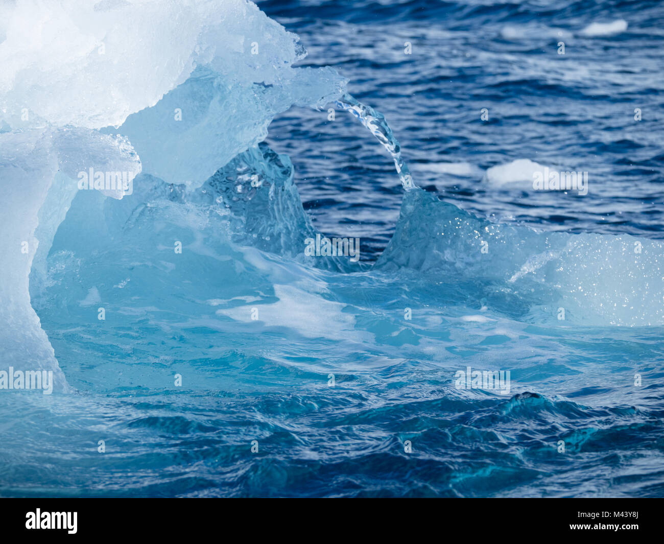 A light, medium and dark blue iceberg floating in the dark gray water ...
