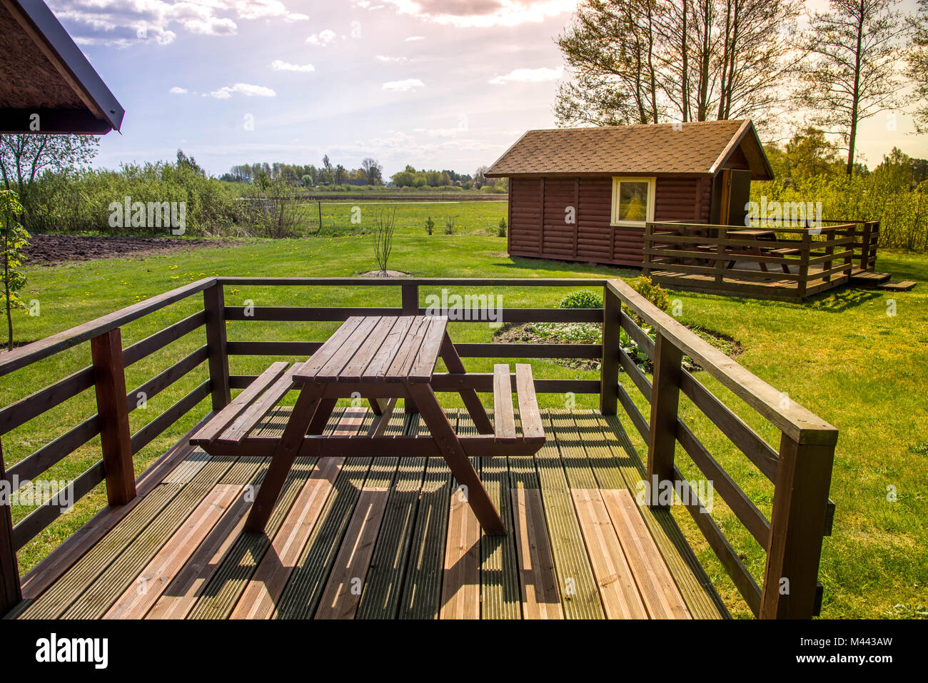 Picnic table on a wooden terrace in garden in early morning. A small ...