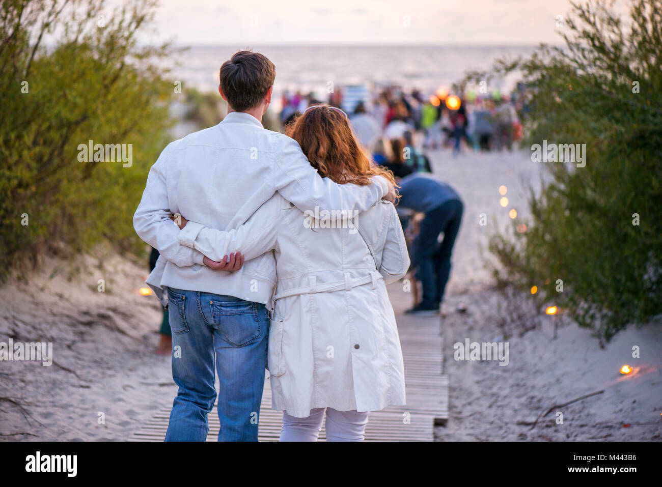 Happy couple hugging and walking on seaside on lit candle path during ...