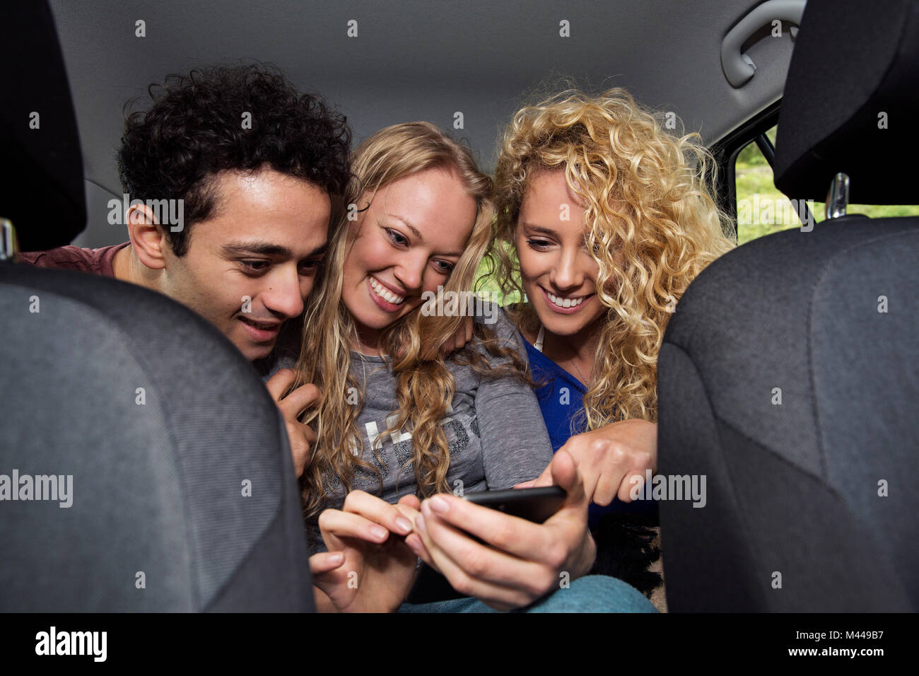 Friends in back seat of car looking at smartphone Stock Photo - Alamy