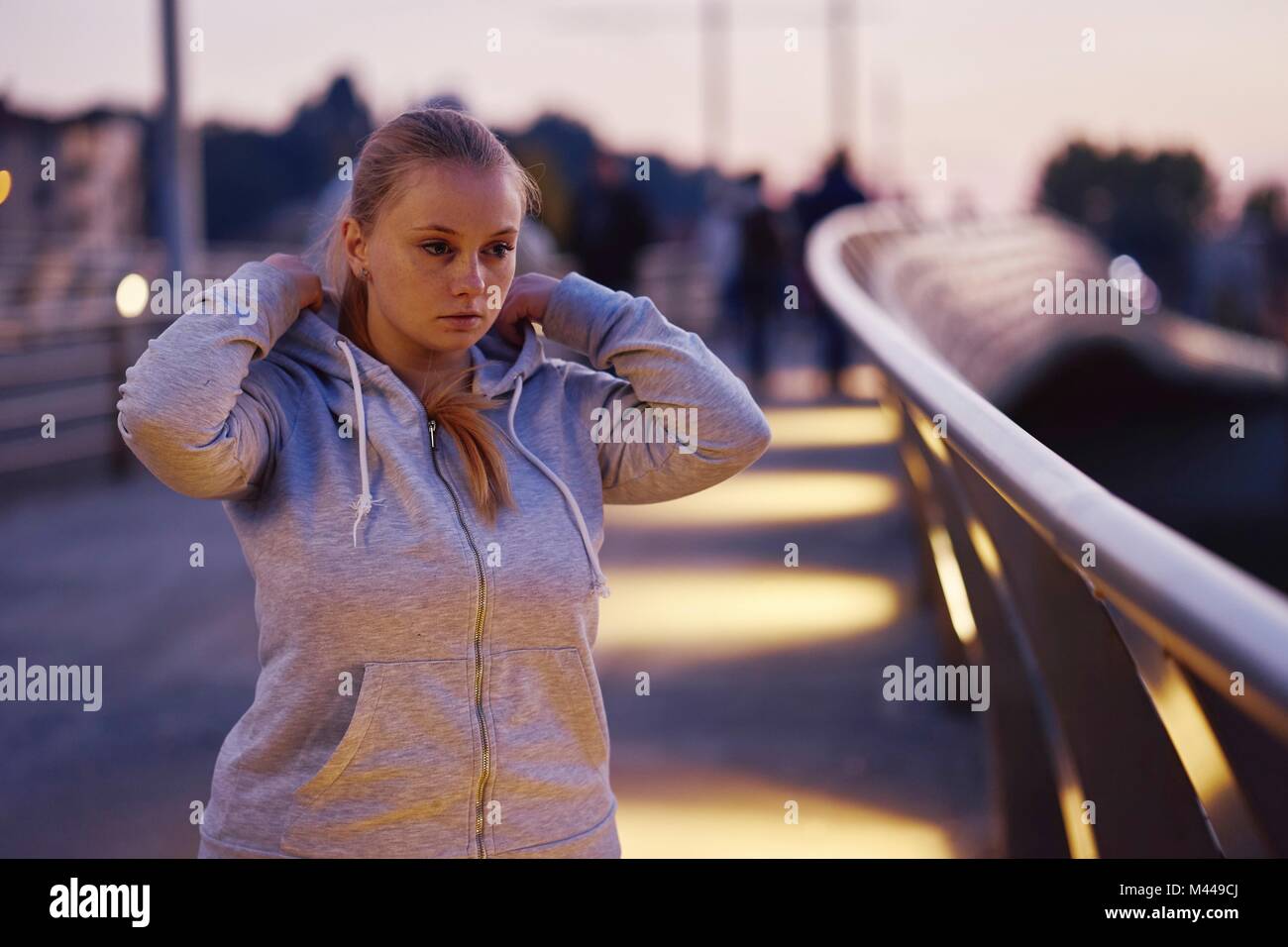 Curvaceous young woman training, getting hoody ready on footbridge at ...