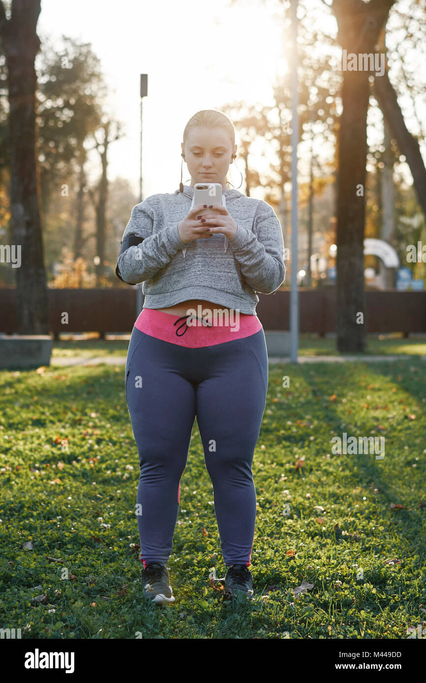 Curvaceous young woman training in park, looking at smartphone Stock ...