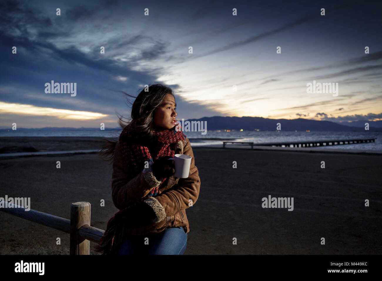 Young woman wrapped in scarf looking over her shoulder from beach at ...