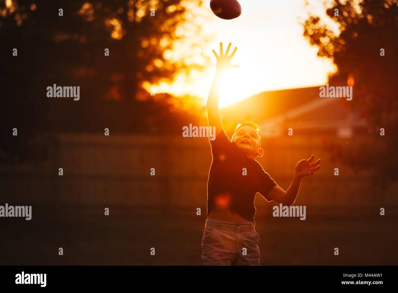 Boy practicing american football in garden reaching to catch ball mid ...