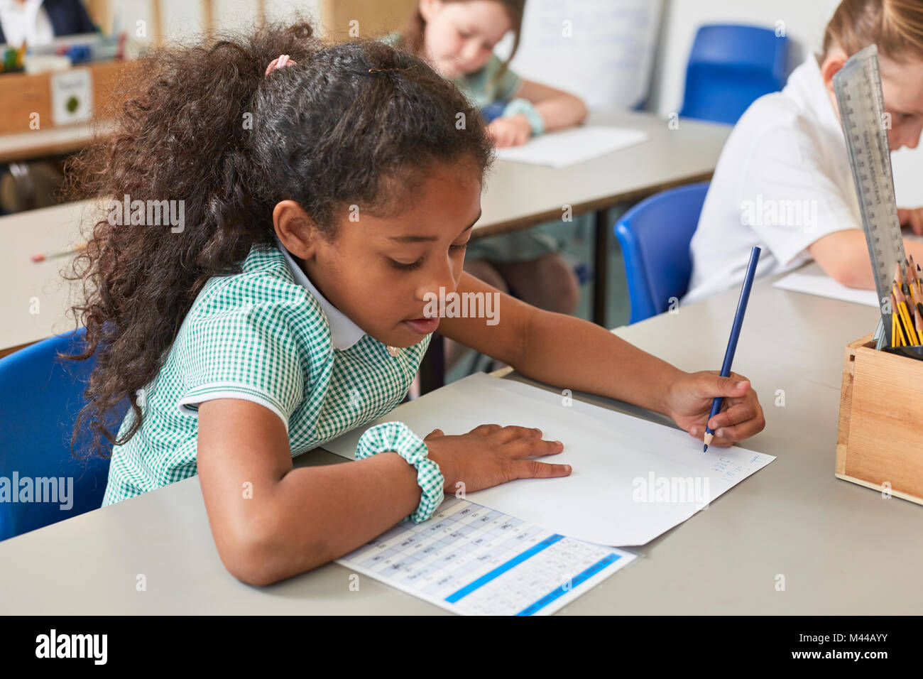 Schoolgirl writing at classroom desk in primary school lesson Stock ...