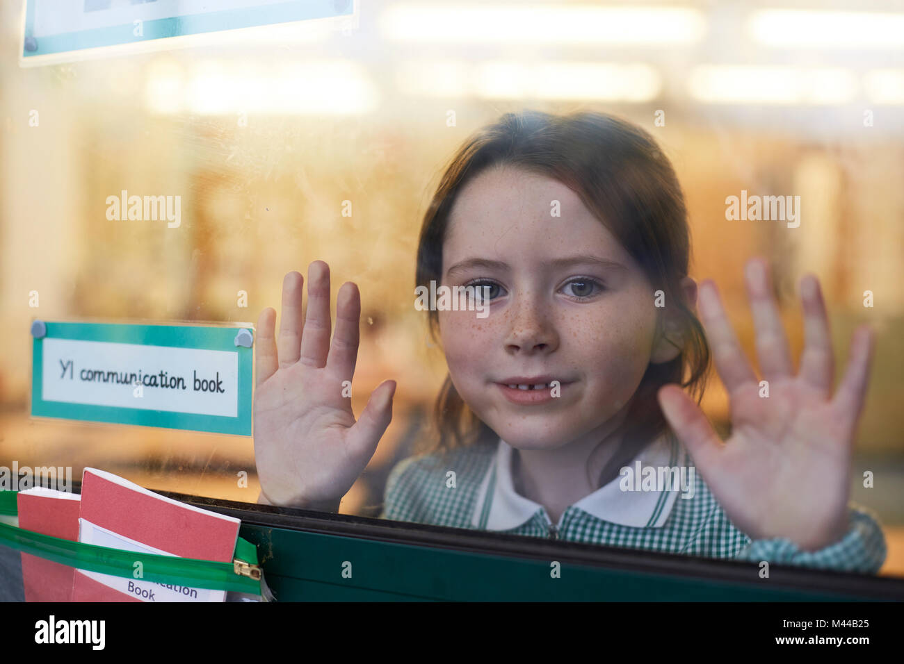 Portrait of schoolgirl with hands on classroom window at primary school ...