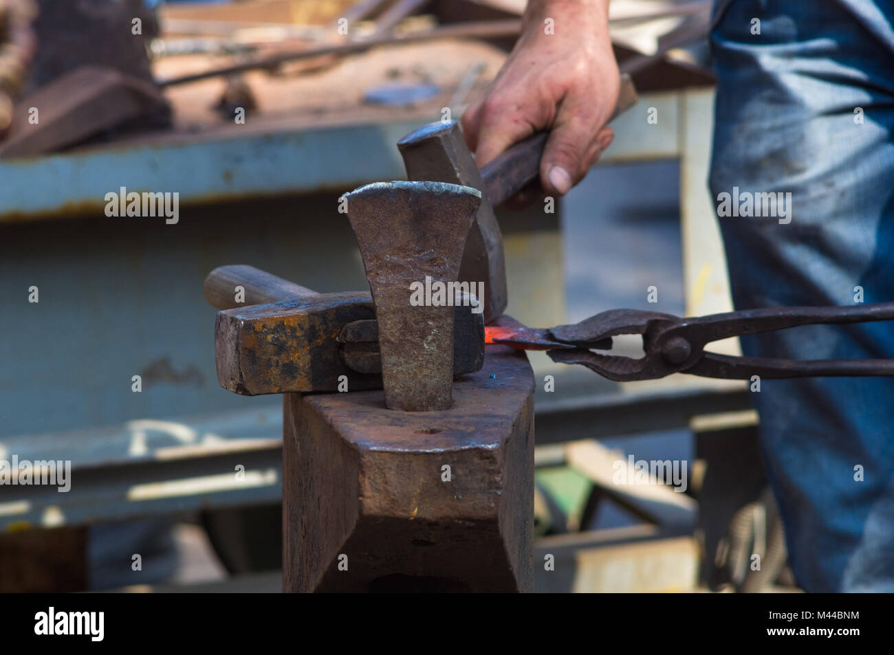 blacksmith performs the forging of hot glowing metal on the anvil ...