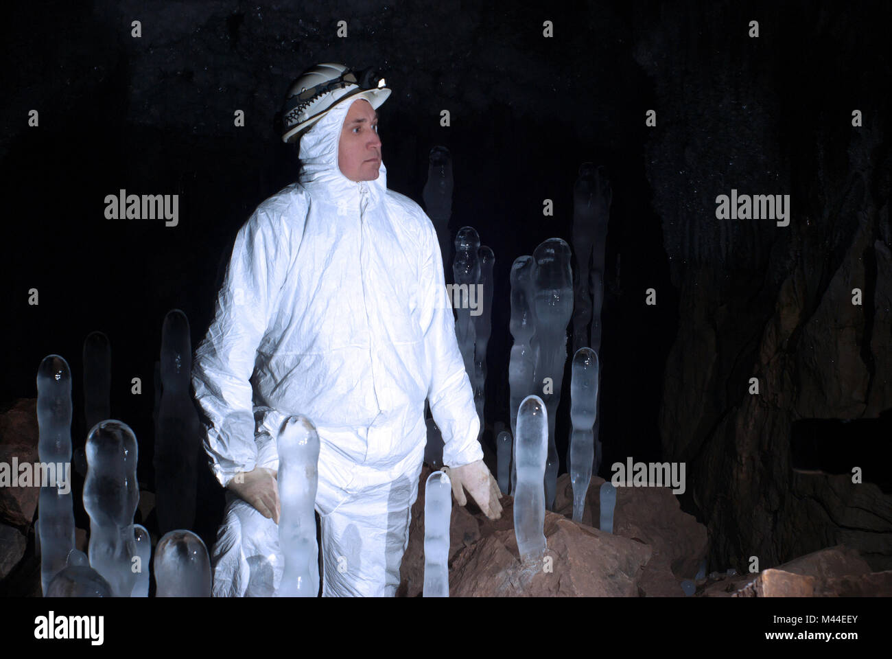 potholer in white overalls among ice stalagmites in a cave on a dark ...