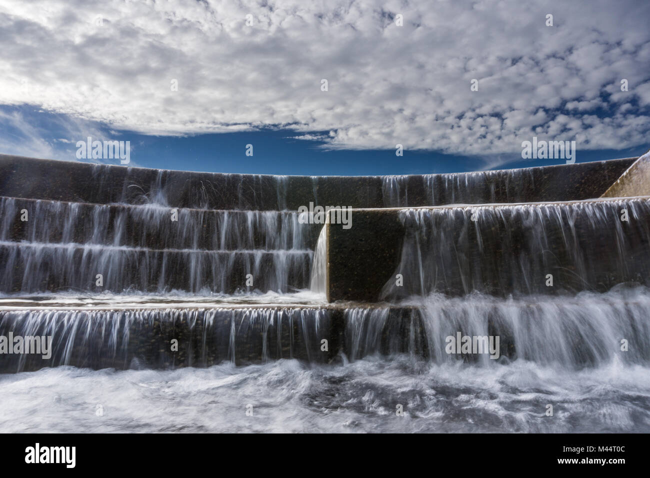Fast running water over stairs with blue sky and white clouds on the ...